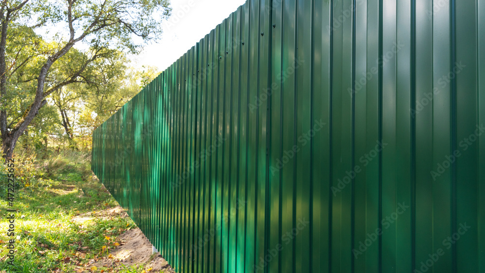 Foto de A corrugated fence of green metal sheets with screw. Texture of ...