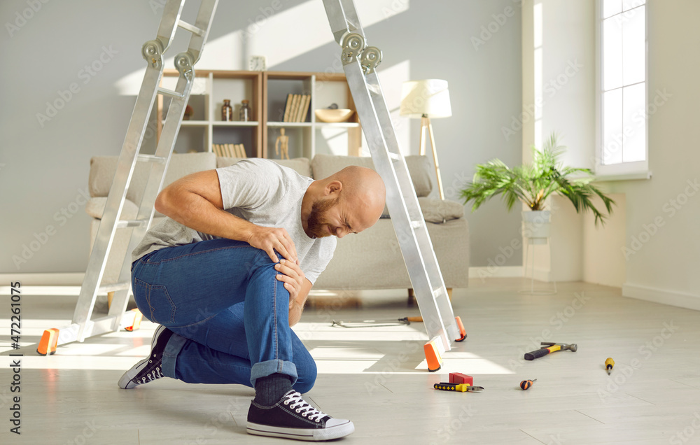 Unlucky man who just fell off ladder at home is sitting on floor and ...