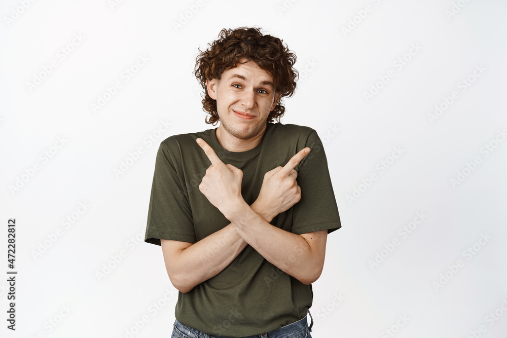 Confused curly-haired man pointing fingers sideways, showing left and ...
