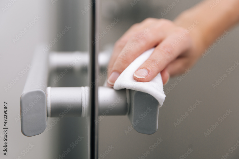 Cleaning glass door handles with an antiseptic wet wipe. Woman hand ...