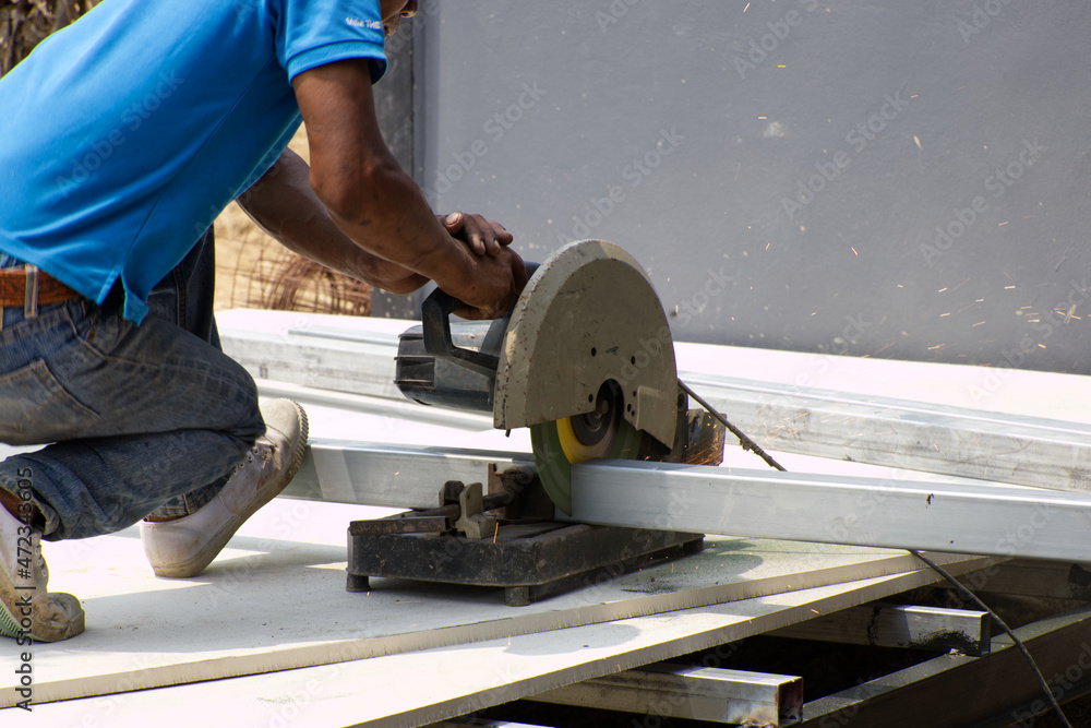 An Asia man in a blue shirt and jeans is cutting metal by using a metal ...