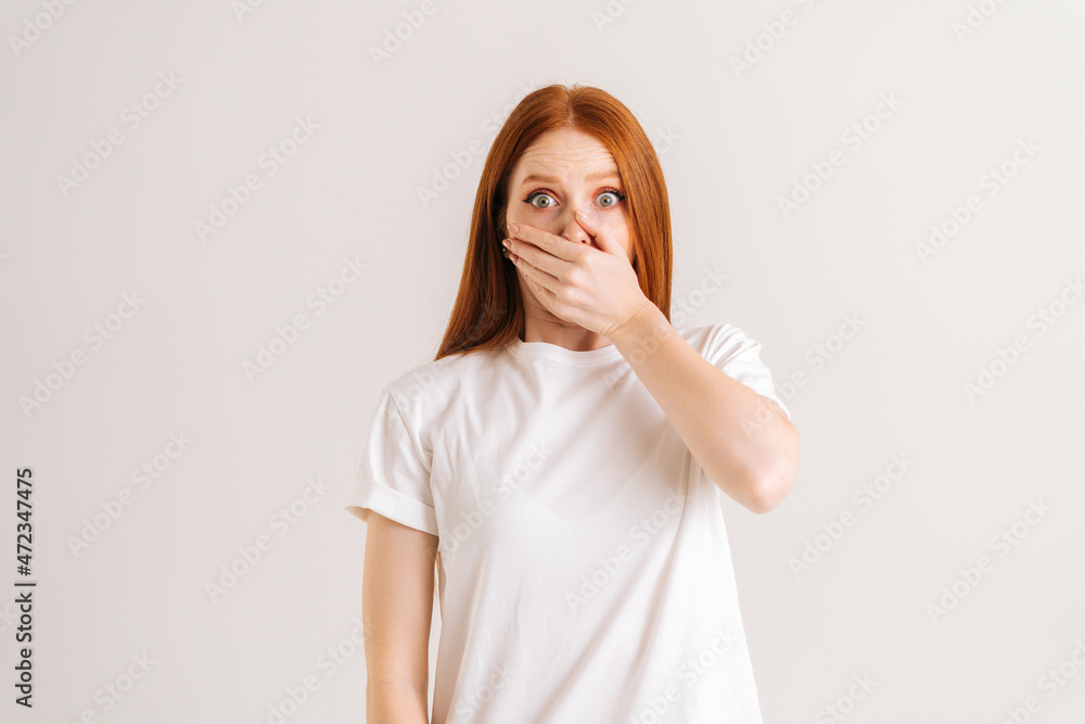 Studio portrait of astonished shocked young woman covering mouth with ...