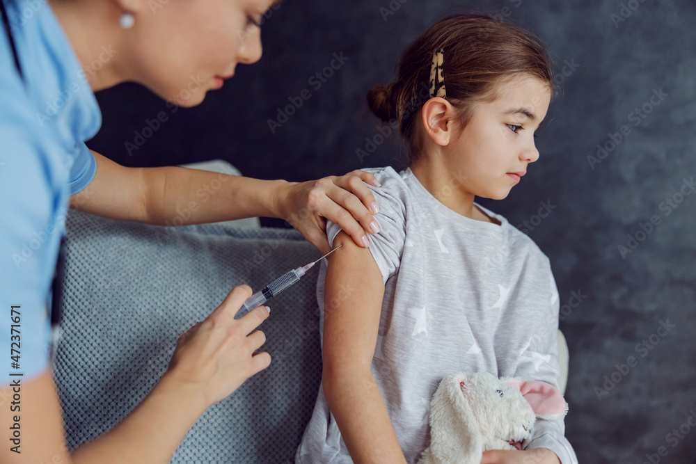 Scared little girl sitting on sofa and getting vaccine. Stock Photo ...