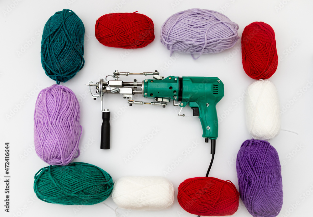 Tufting gun and skeins of yarn of various colors on white background ...
