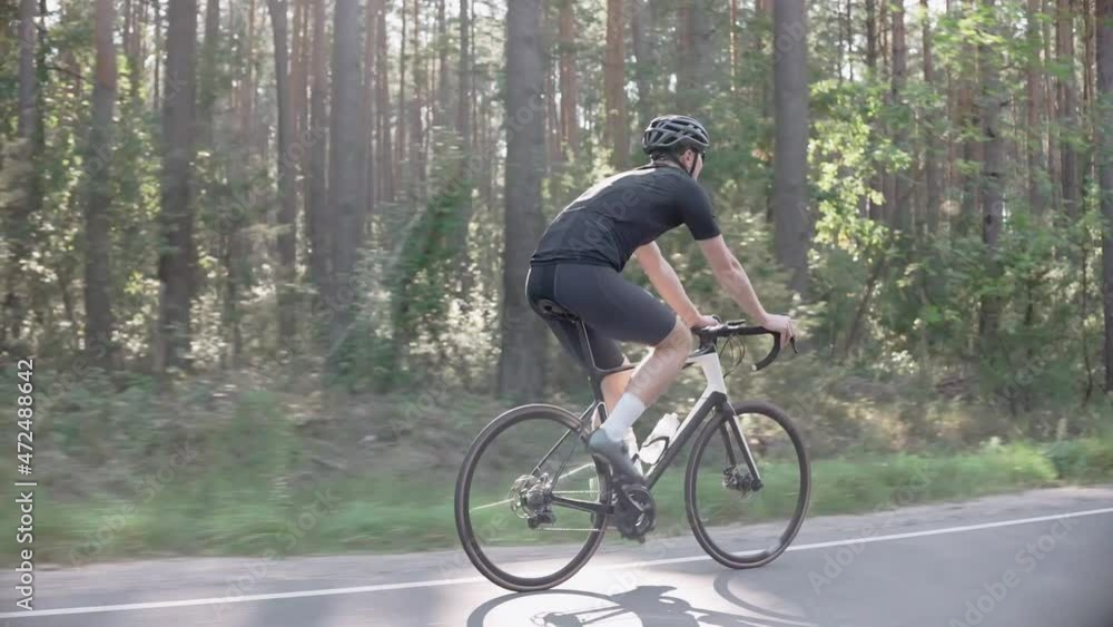 A male cyclist trains by riding a road bike in a sunny pine forest ...