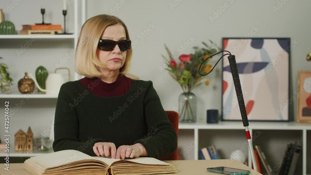 Blind woman reading braille book using fingers, sitting in living room ...