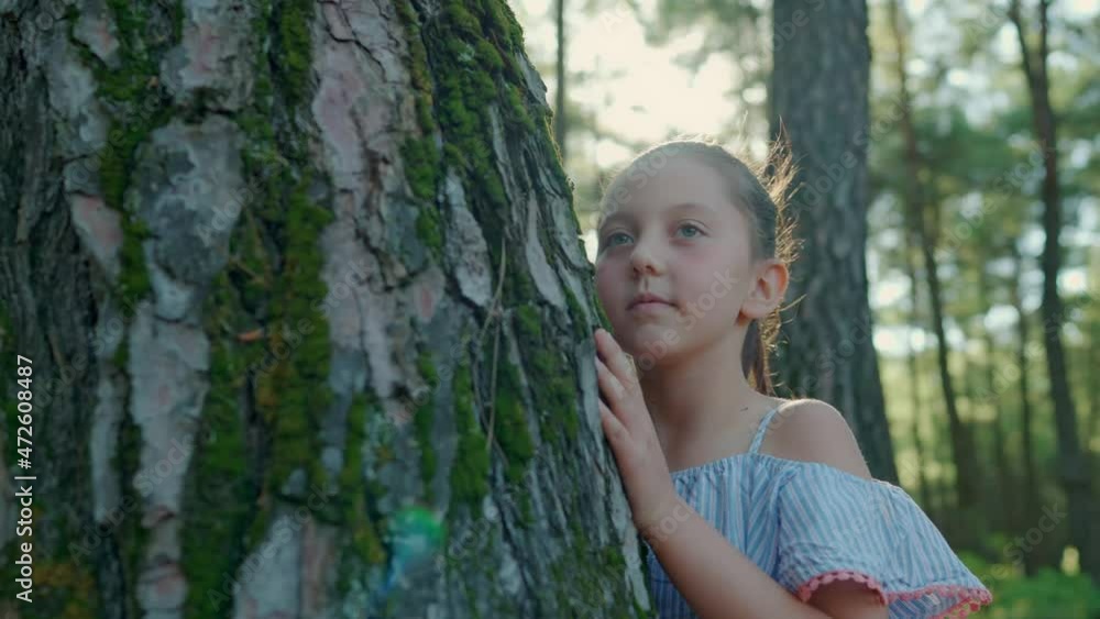 Nature lover little girl hugs an old moss-covered tree on a sunny ...