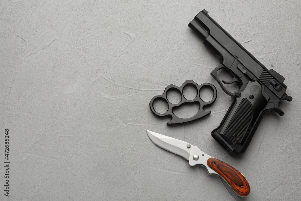 Black brass knuckles, gun and knife on light grey stone background ...