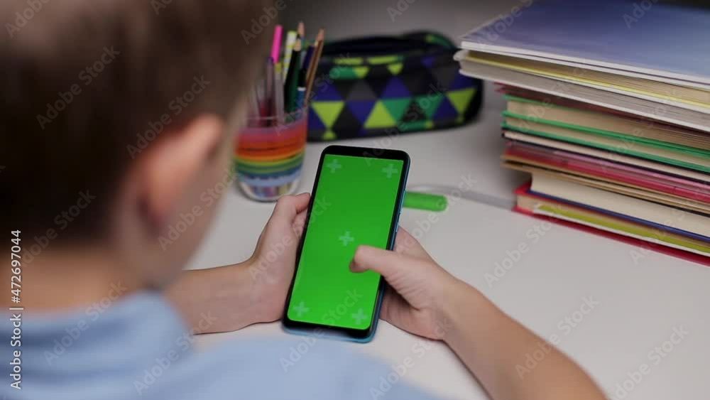 Boy holding a smartphone with a green screen at home, scrolling ...