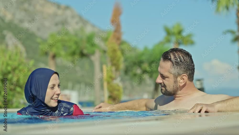 A young woman wearing a hijab swimsuit is swimming in the pool with her ...
