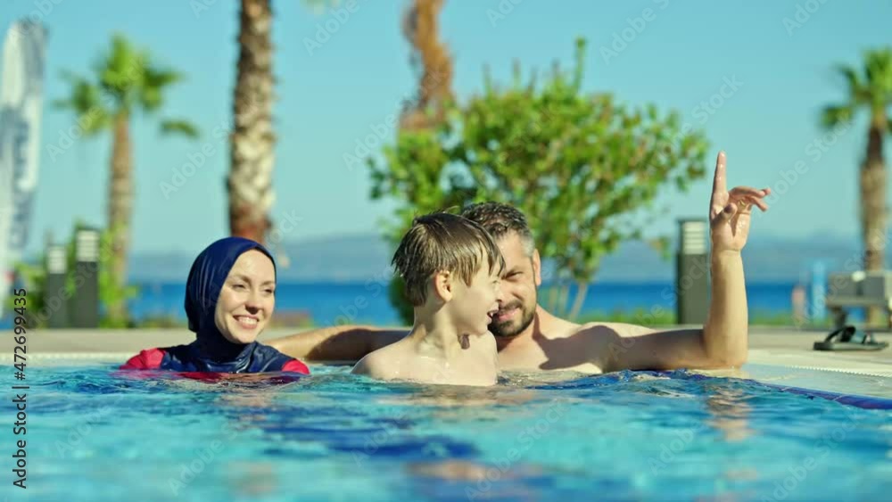 A young woman wearing a hijab swimsuit is swimming in the pool with her ...
