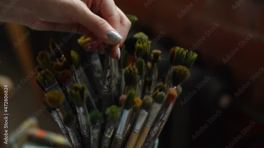 Close-up hands of unrecognizable female artist choosing paintbrush for ...