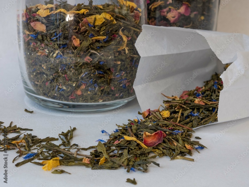 Tea mixture of herbs in a glass jar. The tea leaves are scattered on ...