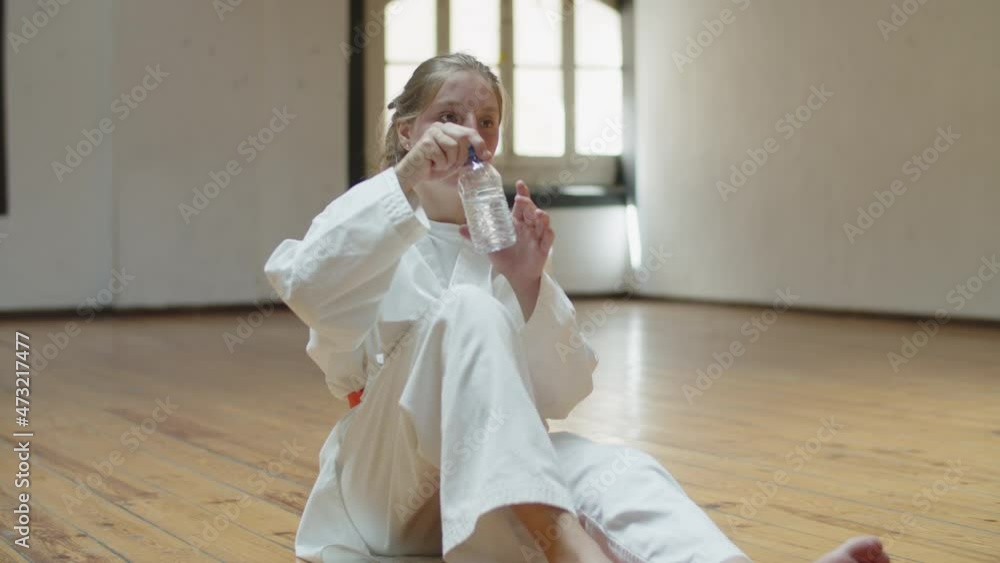 Static shot of tired karateka drinking water in gym. Long shot of ...