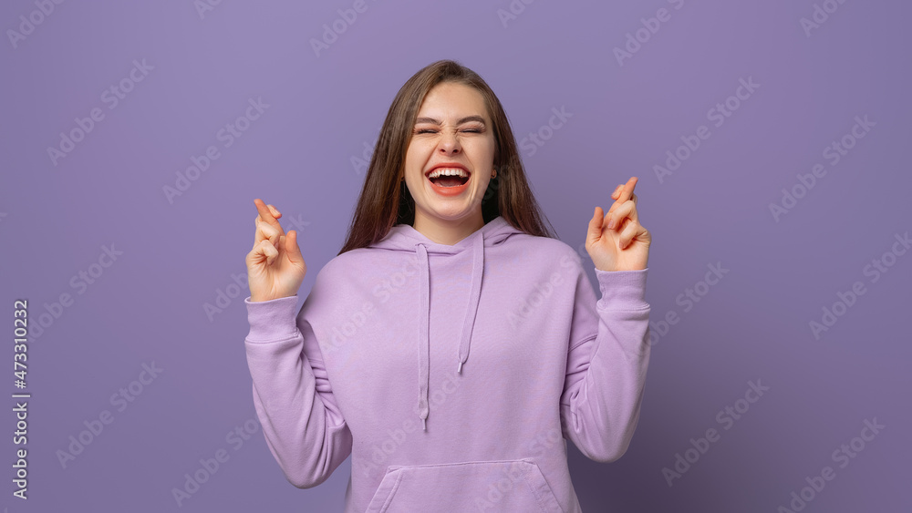 Enthusiastic young woman makes wish with crossed fingers, looking up ...