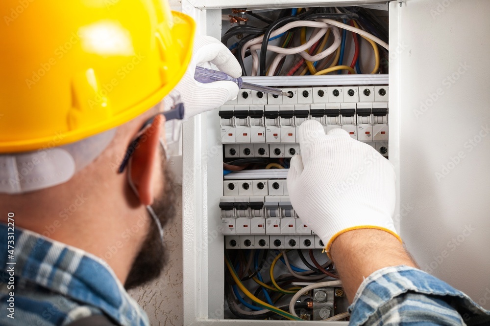 Electrician at work on an electrical panel protected in safety goggles ...
