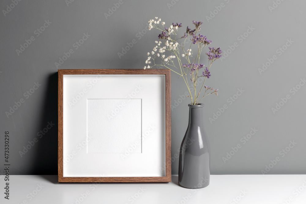 Square wooden frame with passepartout over grey wall with dry flowers ...
