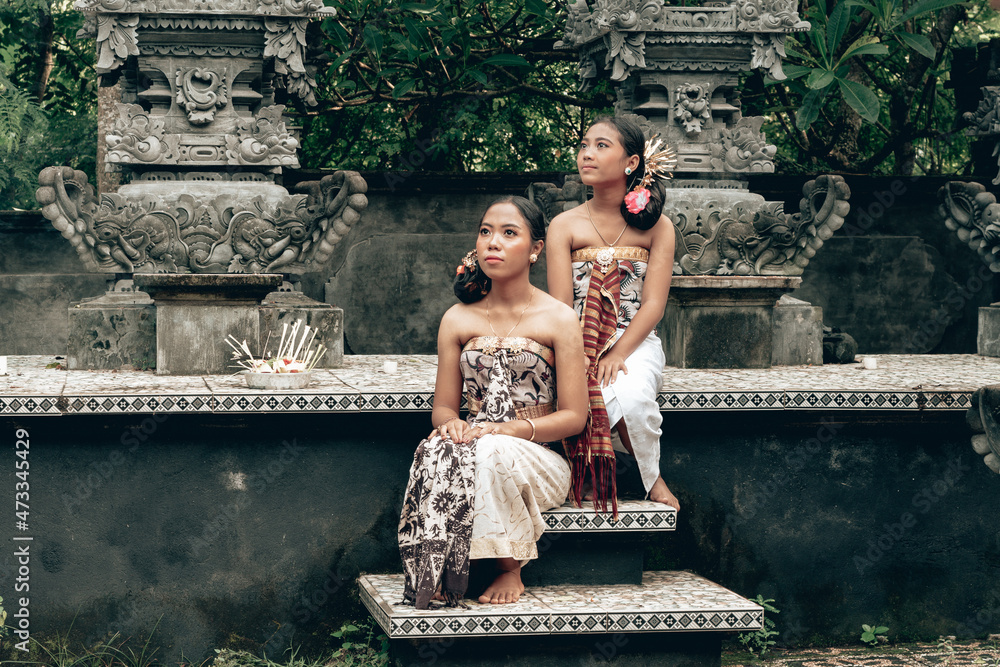 Two young Balinese girls in a Hindu temple in Bali with incense sticks ...