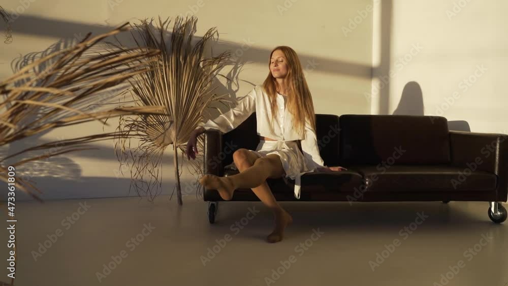 Young girl with long hair in white dress and pantyhose sits on black ...