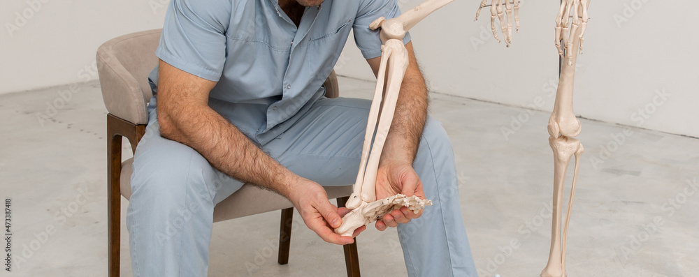 Doctor man pointing on leg of human skeleton anatomical model ...