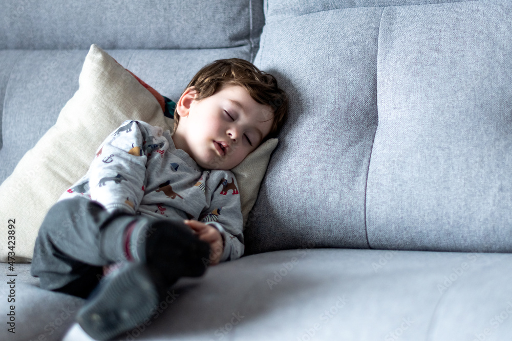 A little boy sleeping sitting on the gray sofa leaning on a cushion and ...