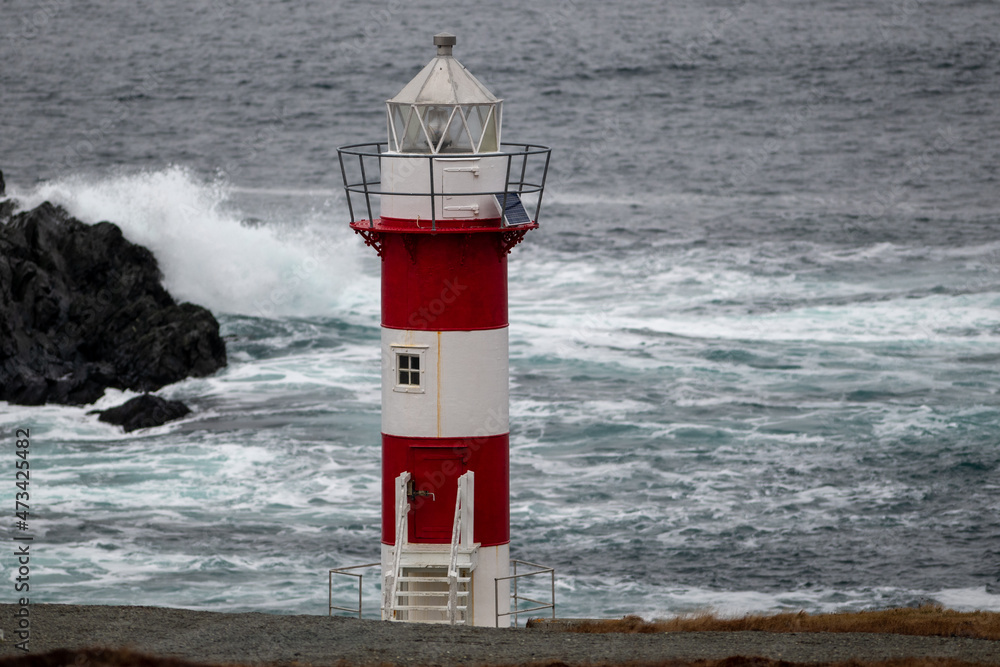 A tall circular lighthouse tower has horizontal red and white colors ...