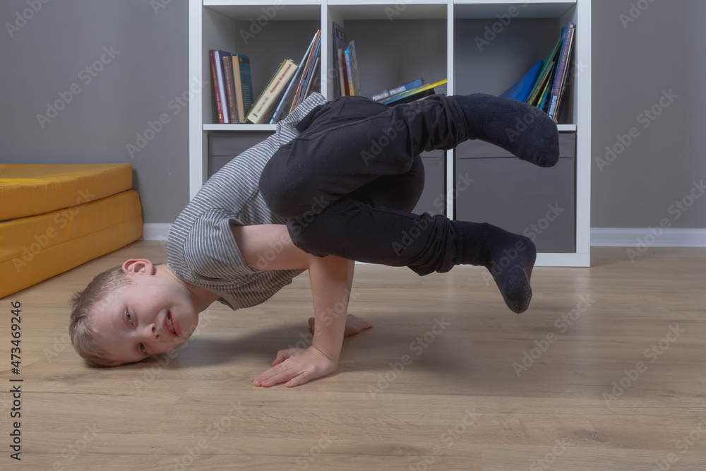 A 7-year-old caucasian boy is dancing breakdancing at home on the floor ...