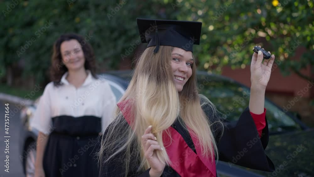 Proud graduate woman boasting car key standing outdoors with blurred ...