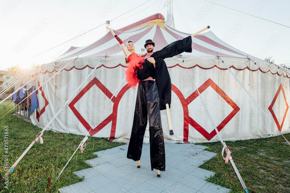 Male artist carrying female performer with stilts at circus tent ...