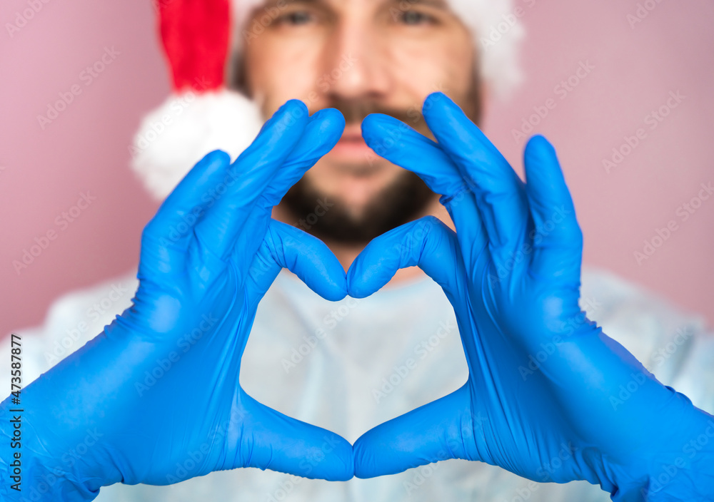 Doctor with a beard in a santa hat and in medical gloves shows the ...