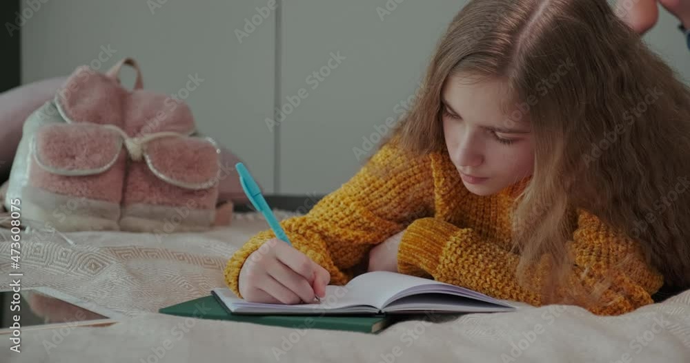 Teen girl writing in note book, lying on the bed, resting in her ...