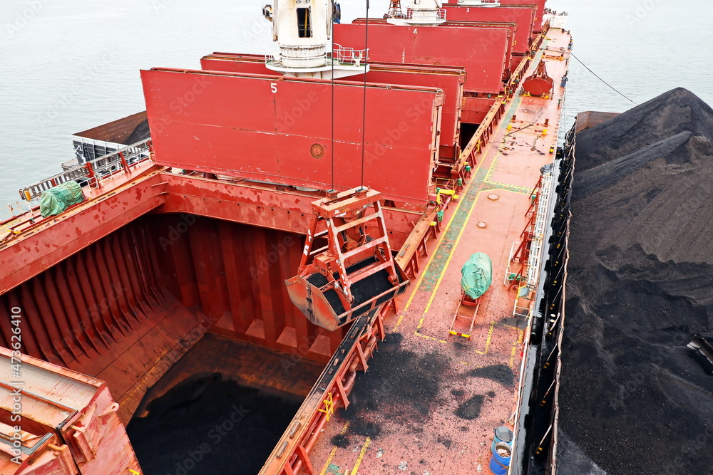 Loading coal from cargo barges onto a bulk carrier using ship cranes ...