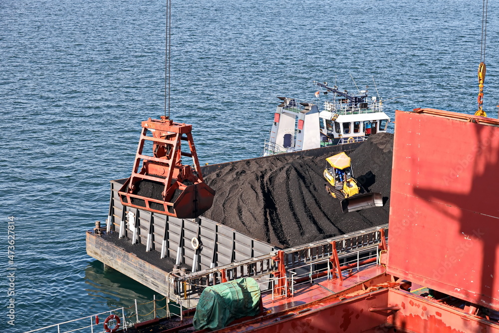 Loading coal from cargo barges onto a bulk carrier using ship cranes ...