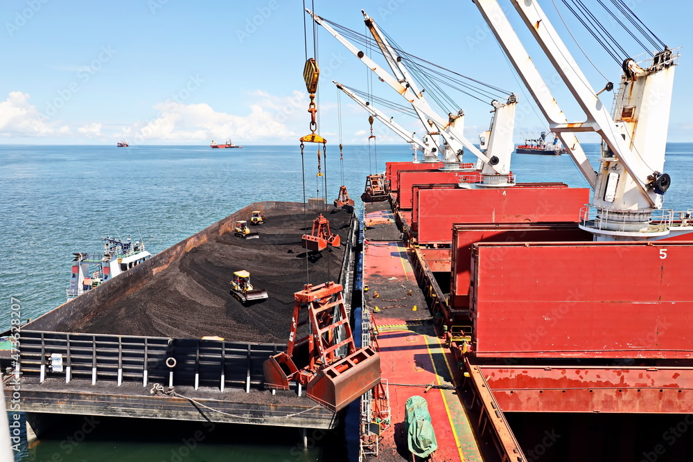 Loading coal from cargo barges onto a bulk carrier using ship cranes ...