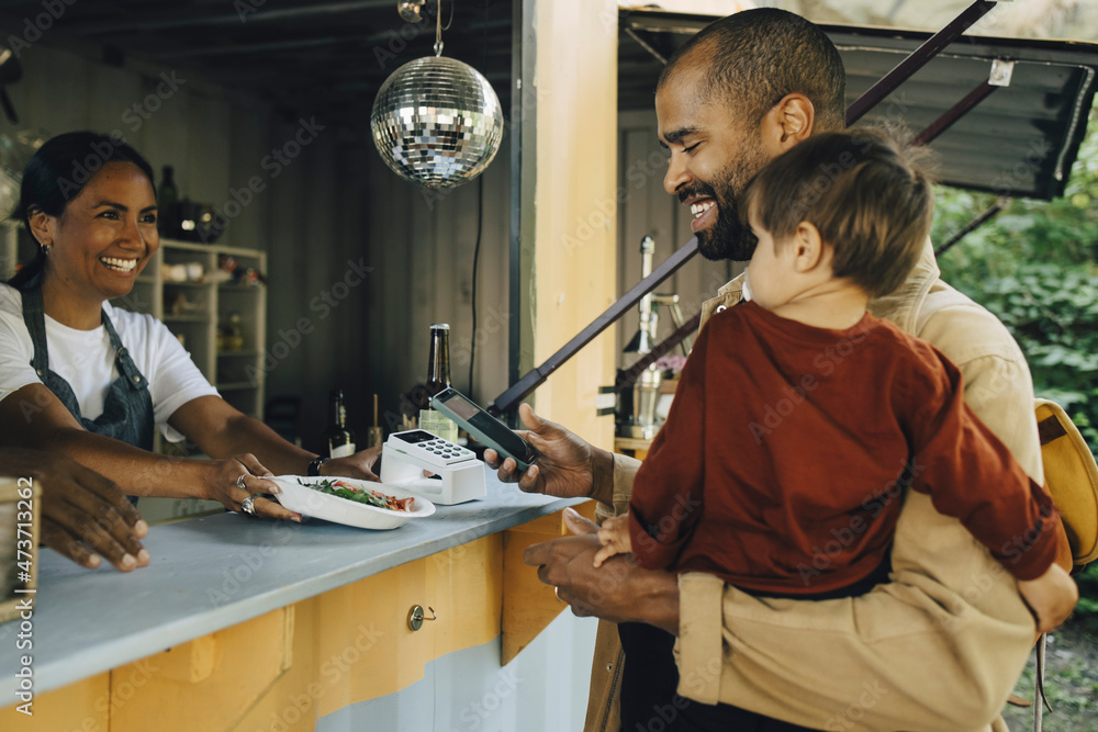 Smiling male customer with son doing contactless payment through smart ...