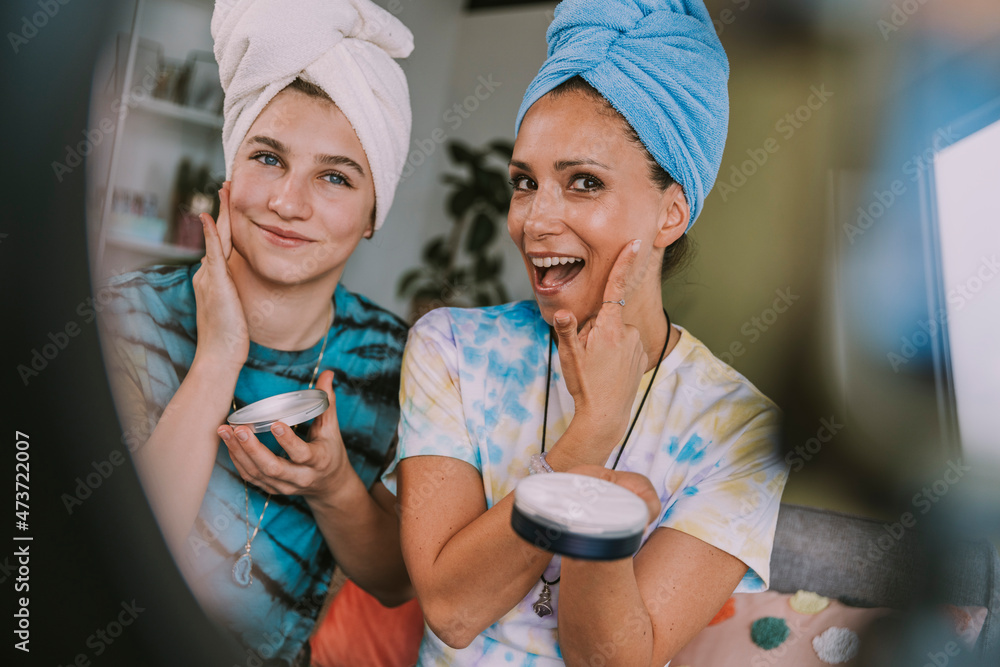 Smiling female influencers applying face cream while vlogging at home ...