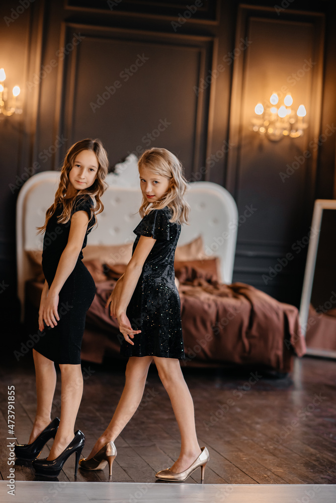 Two beautiful little girls in black dresses on mother's heels are ...