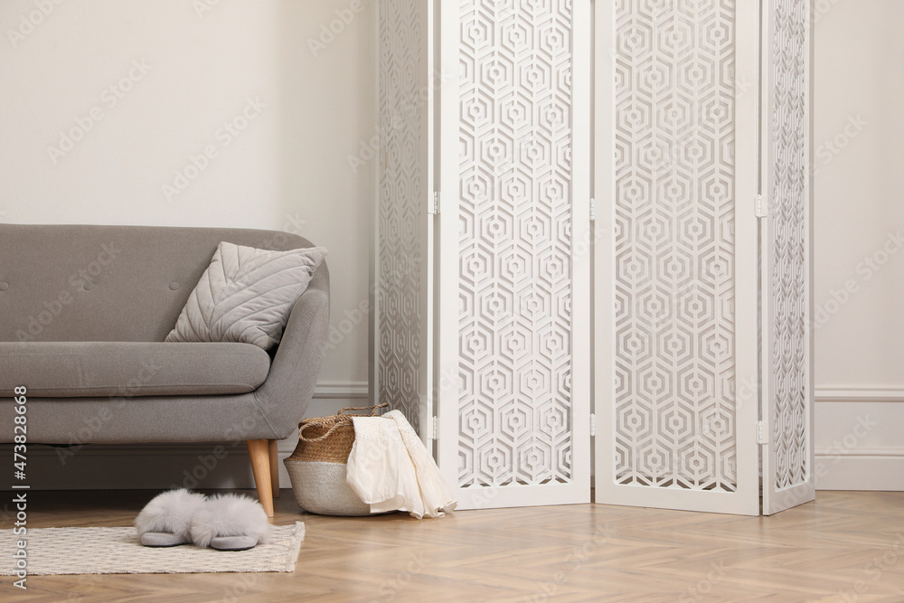 Stylish room with folding screen and sofa near white wall. Interior ...