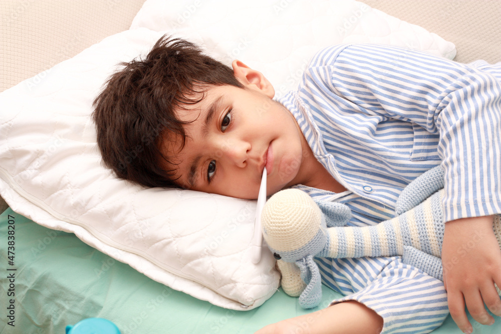 Sick boy with thermometer laying in bed. Sick child with fever and illness in bed. Flu. Cold ...