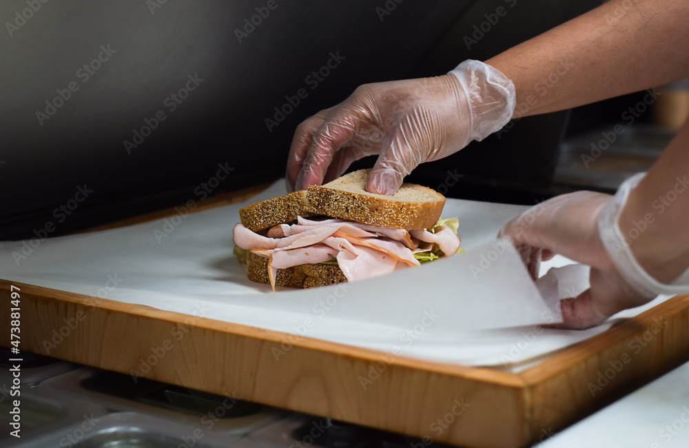 Restaurant kitchen employee wrapping freshly made sandwich for customer ...