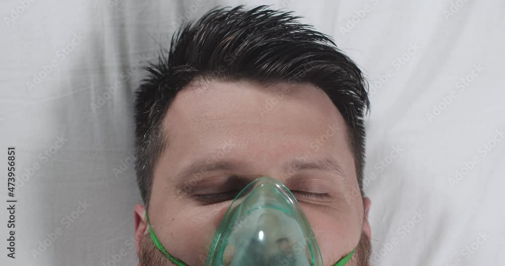Close-up of a young man opening his eyes in a hospital bed in an ...