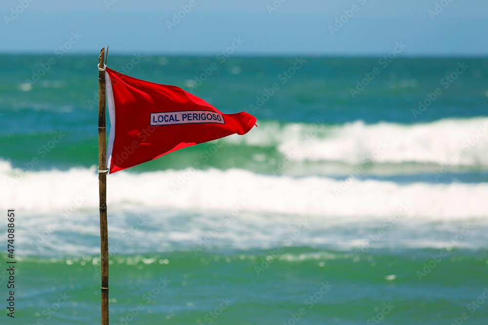 Red flag lifeguard danger warning sign on the beach. No swimming it's ...