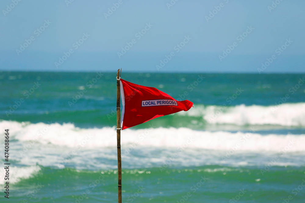 Red flag lifeguard danger warning sign on the beach. No swimming it's ...