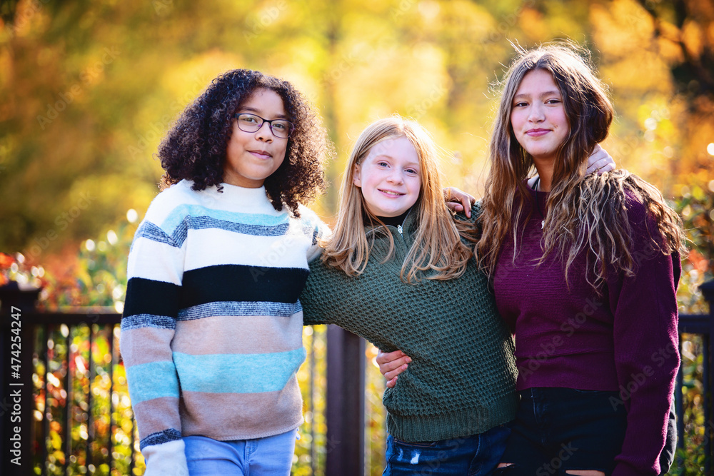 Three pretty tween girls laughing together outdoors in fall colors ...