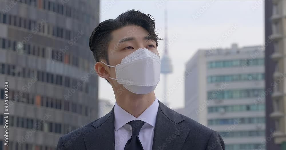 Outdoor hero shot of bold Asian male wearing mask and suit, looking up ...