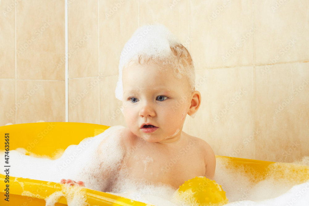 Little baby takes a bath in a yellow bath with bubbles and foam. The ...