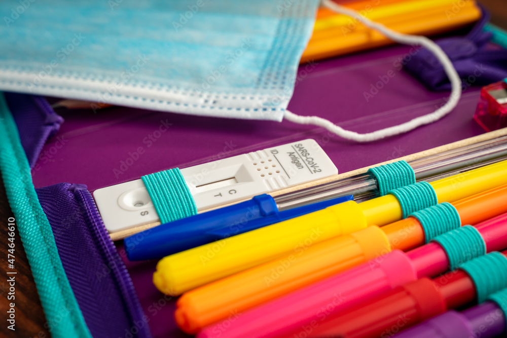 Covid-19 rapid test at school next to mask and crayons in a pencil case ...