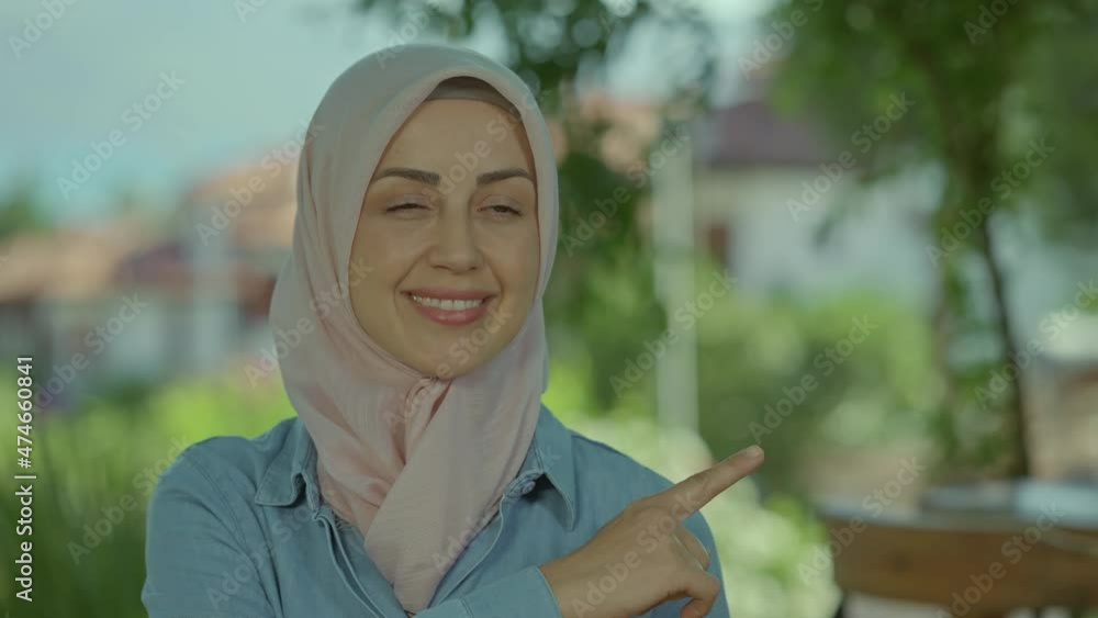 A young woman in hijab, smiling, points her finger to the right of the ...