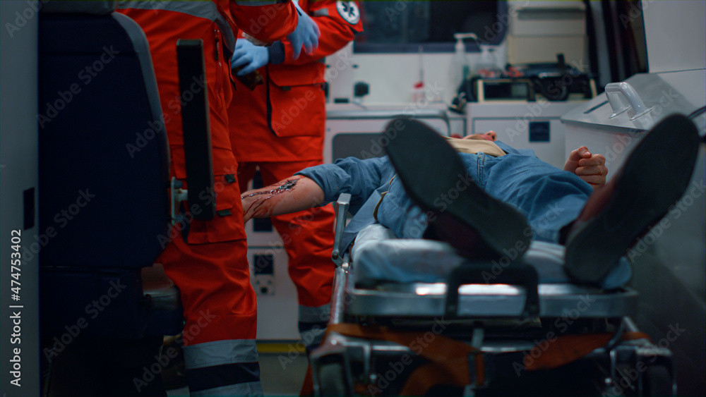 EMS paramedics treating patient with wound on hand in emergency car ...