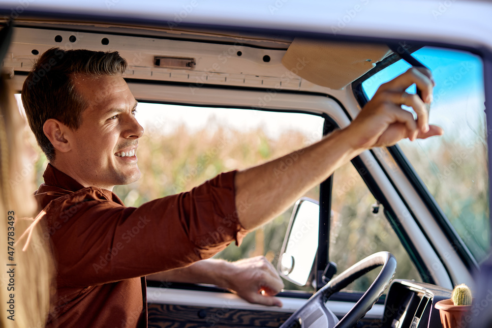 young smiling man fixing the car mirror, side view. handsome guy in ...